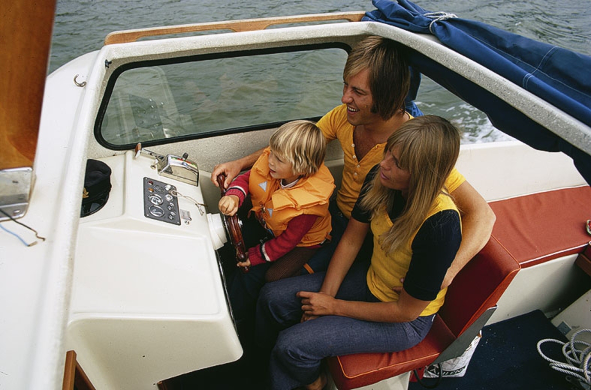 Man med två barn vid styrplatsen på Albin 21. Marknadsföringsbild ...