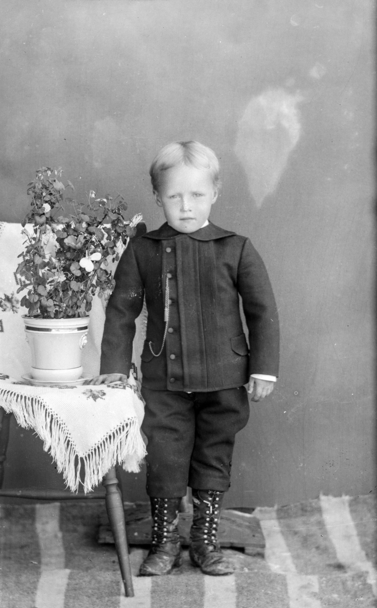 Liten gutt som står ved siden av stol som er pyntet med duk og blomster ...