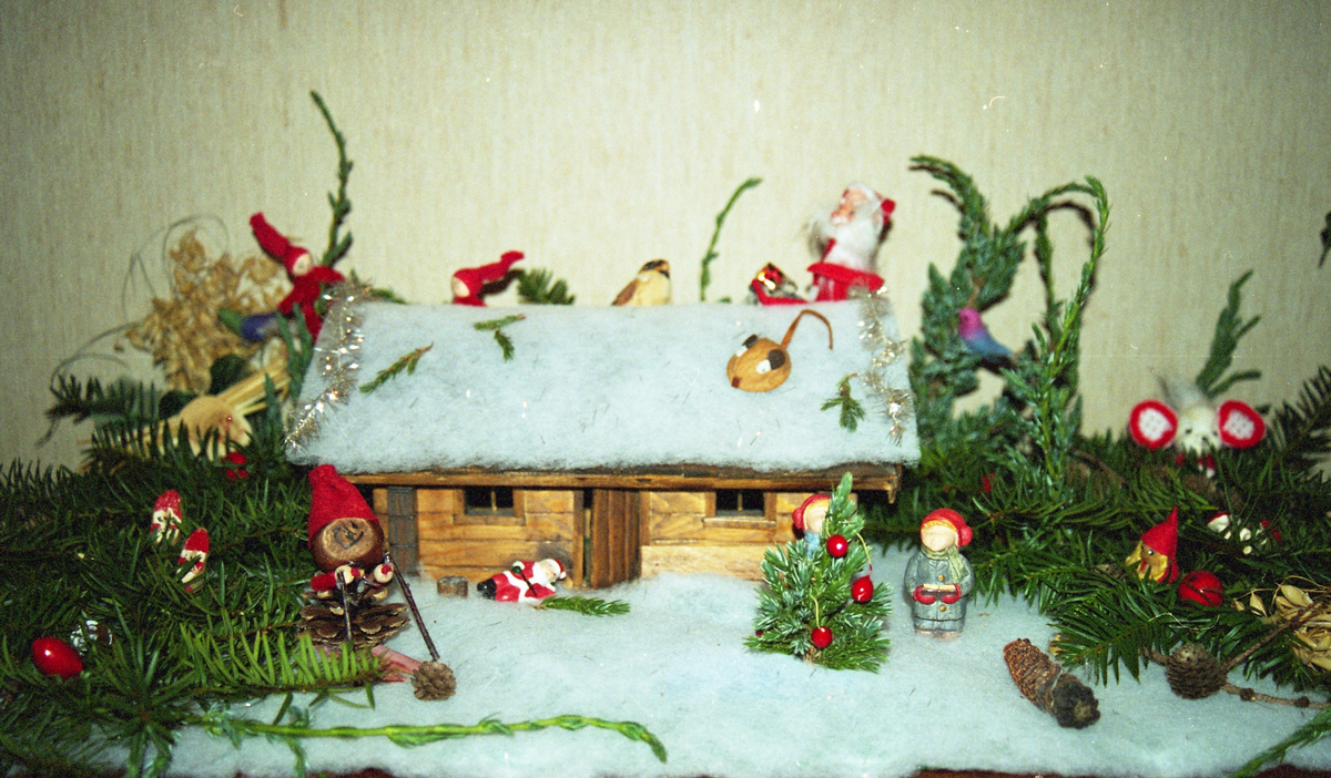Eit lite julepynt-tablå: eit lafta hus med trær av granbar rundt. "Snø ...