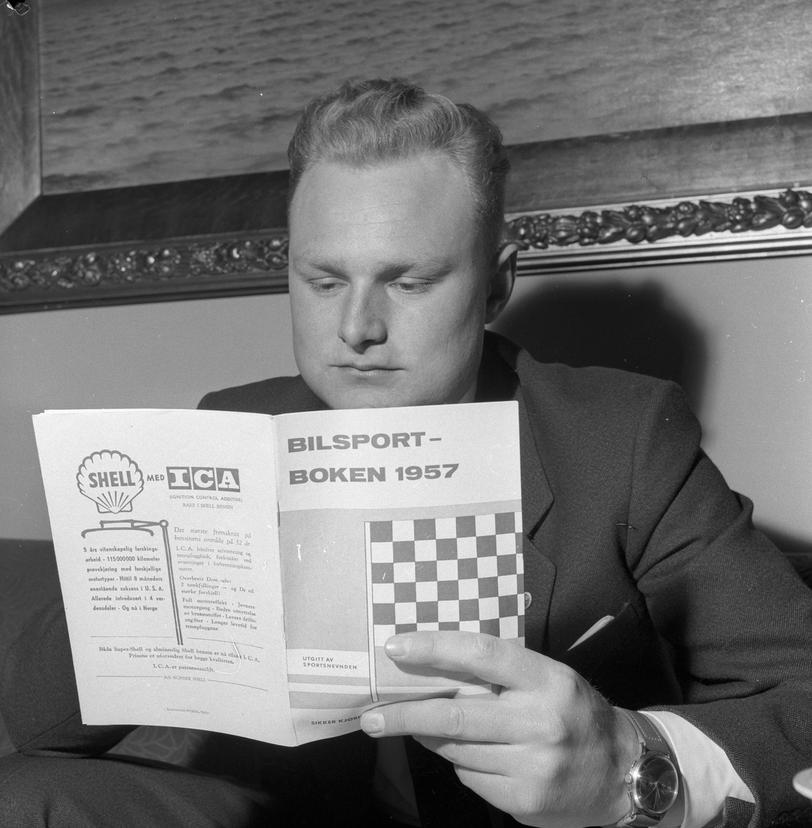 Isracerkjører Edgar Haugen sitter og leser i magasinet "Bilsportboken 1957". Fotografert 28 ...