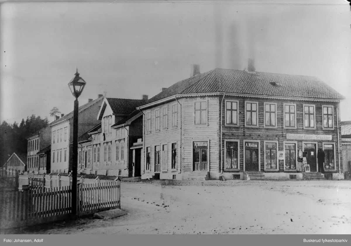 N. Torg i Hønefoss mot Hammerbrogata A. Nilsen, Herrekleder, kåper og ...