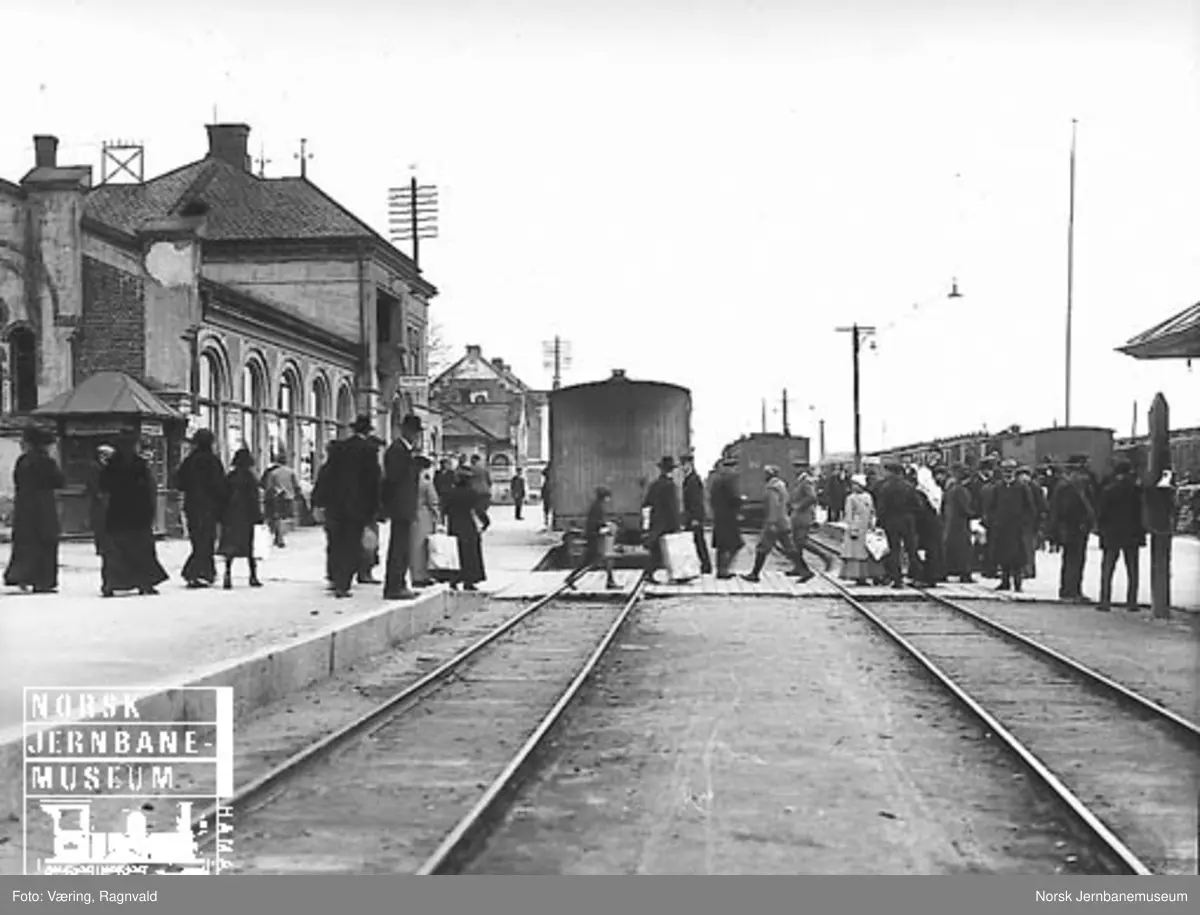 Hamar stasjon med reisende på planovergangen mellom spor 1 og 3 : tog i ...